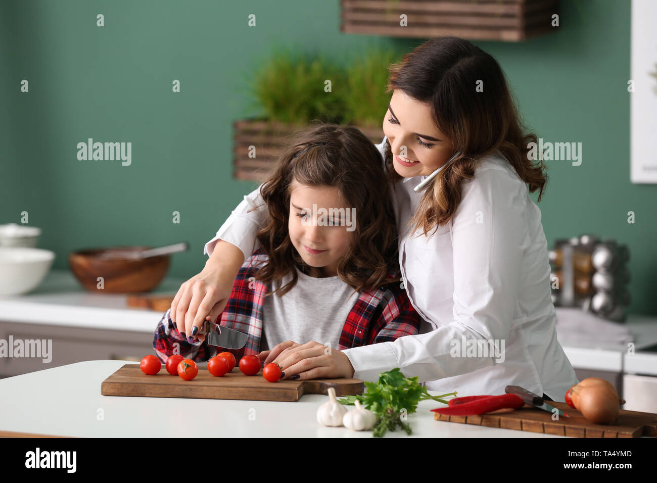 Busy mother cooking with daughter while working at home Stock Photo - Alamy