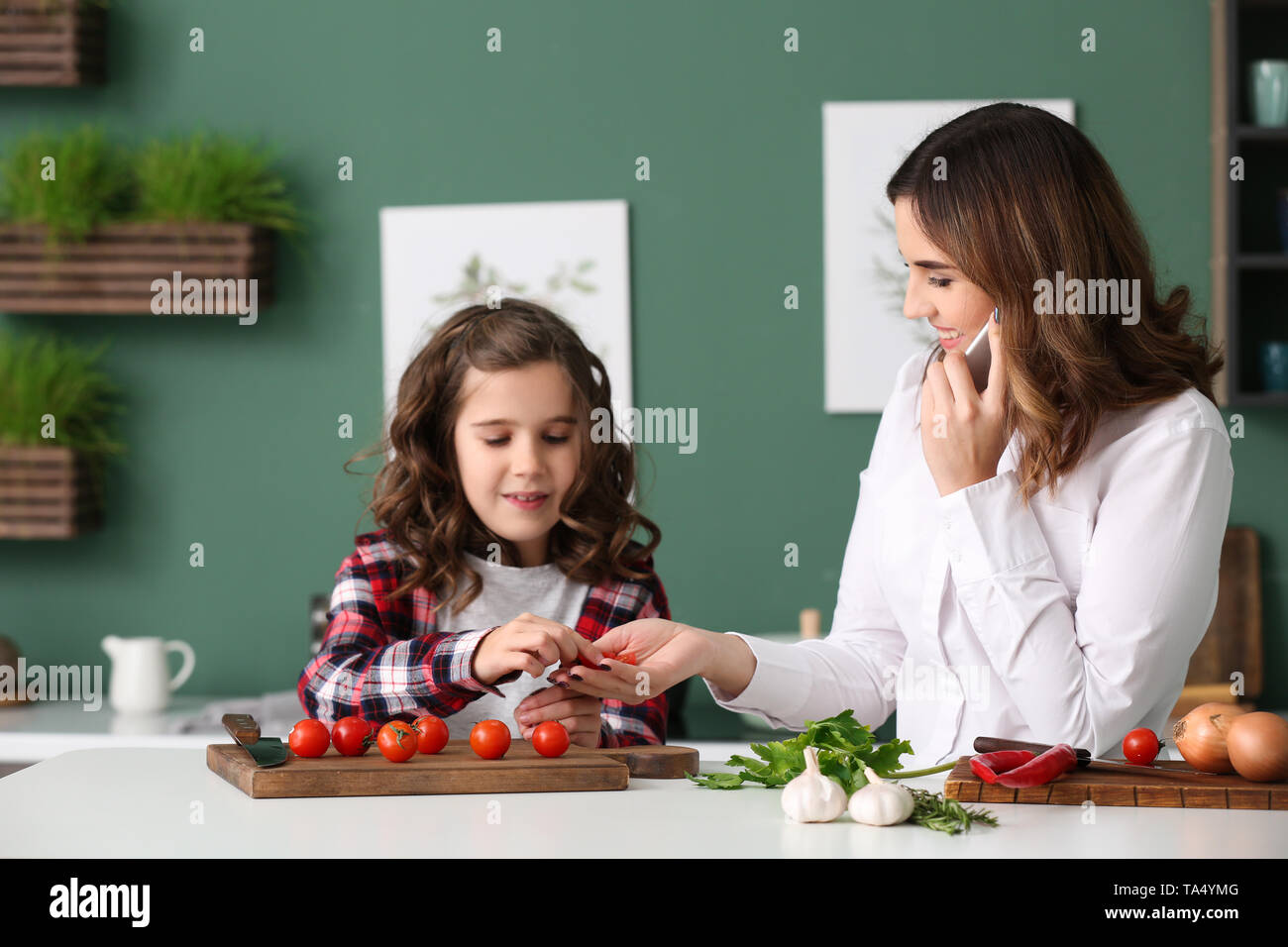Busy mother cooking with daughter while working at home Stock Photo - Alamy
