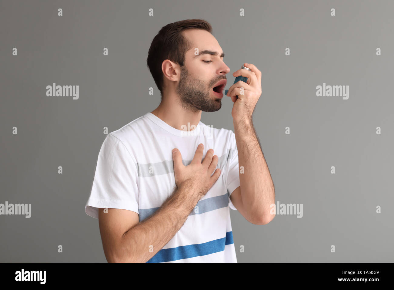 Young man with inhaler having asthma attack on grey background Stock ...
