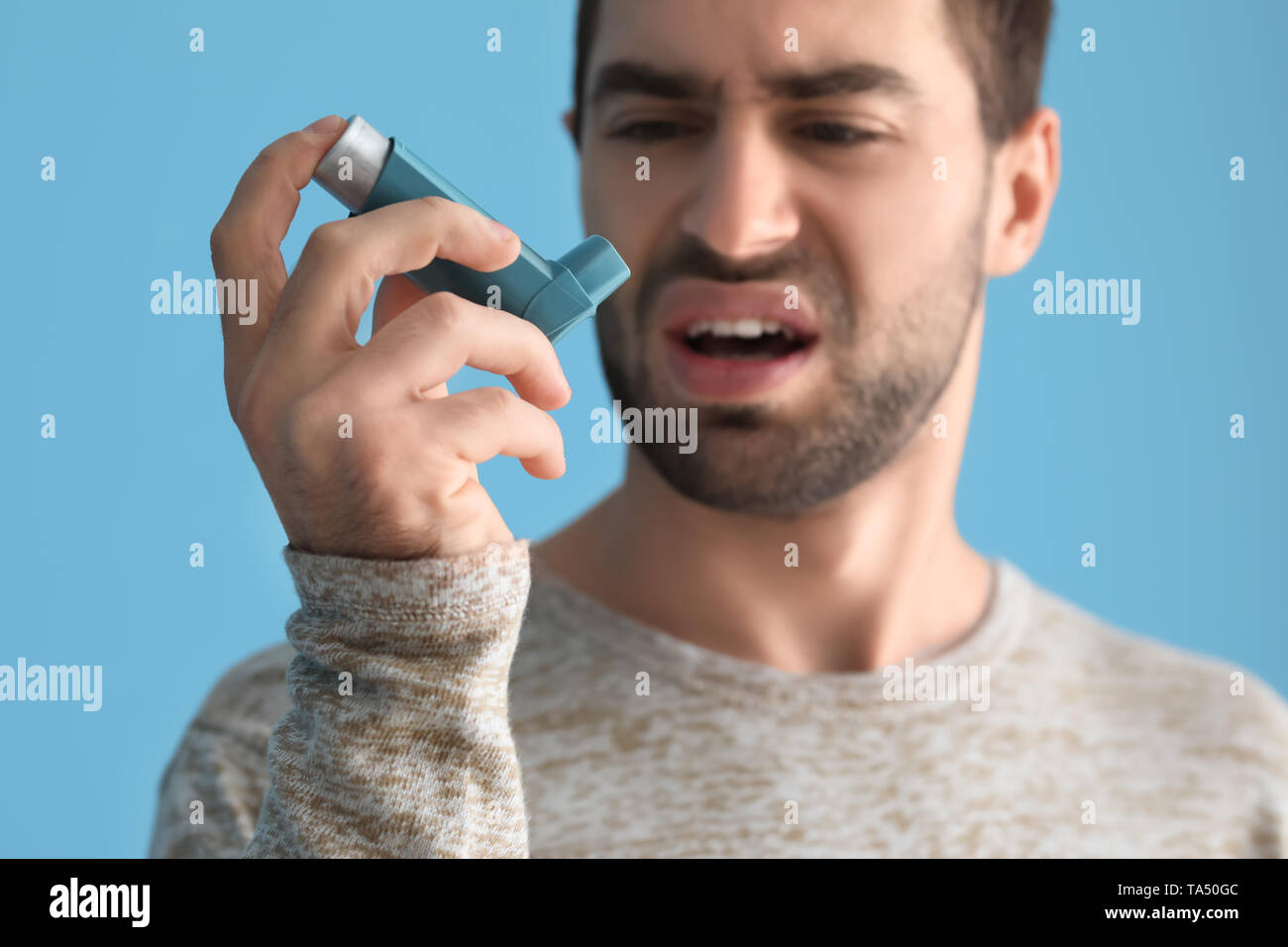 Young Man With Inhaler Having Asthma Attack On Color Background Stock