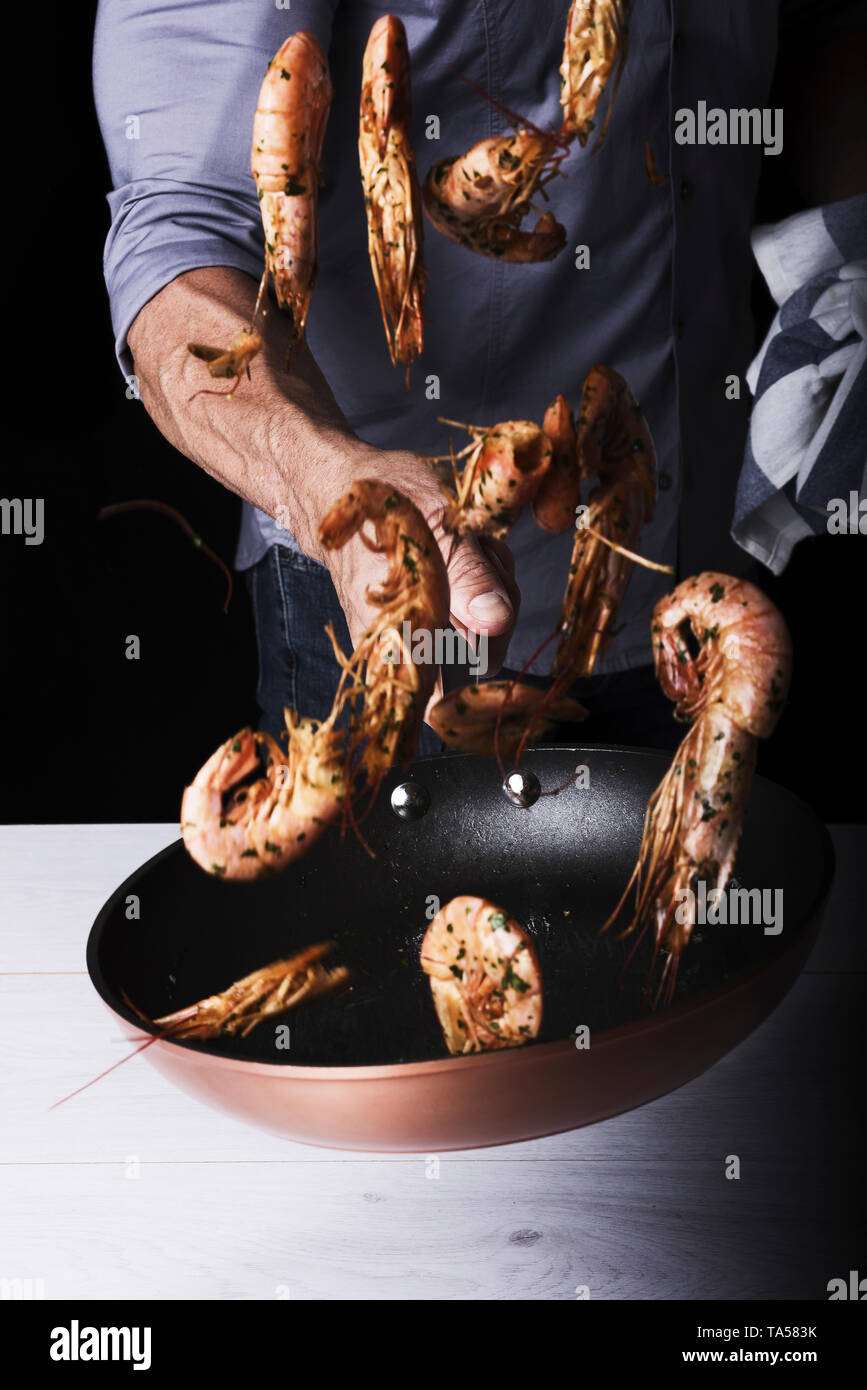 Man makes jumping shrimp in the pan, on a dark background Stock Photo ...