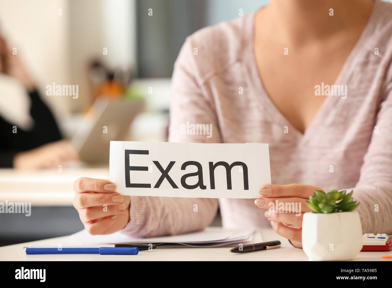 Girl holding paper with word EXAM in classroom Stock Photo - Alamy
