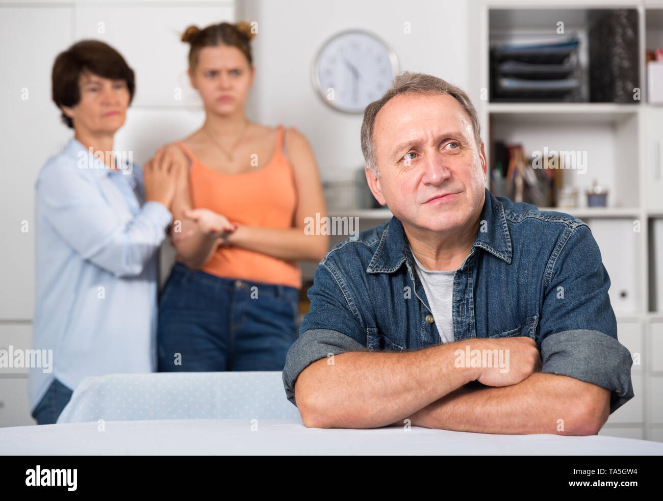 Woman and her daughter are sympathying their sad father who is sitting ...