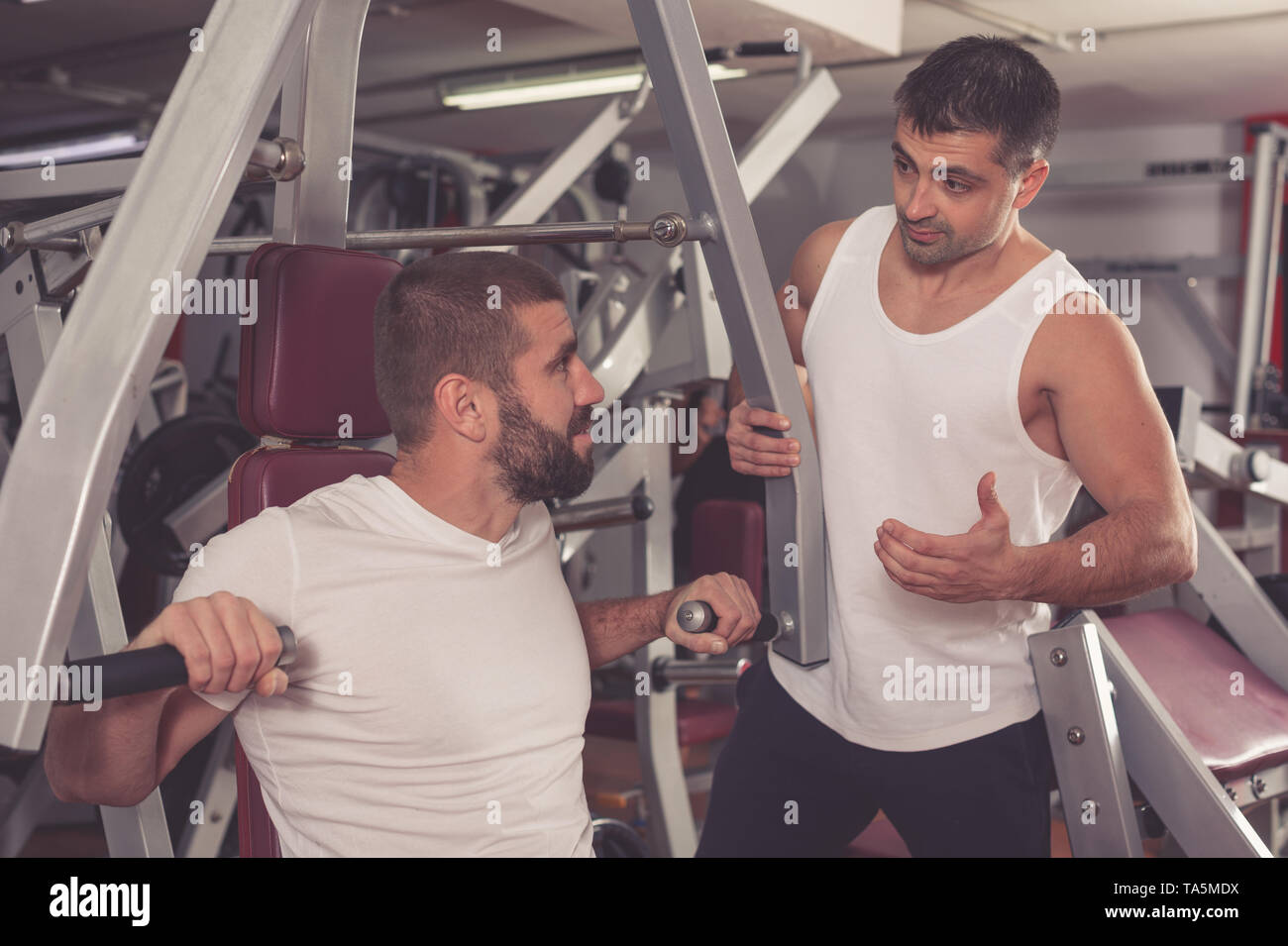 Male trainer explaining to muscular guy technique of performing ...