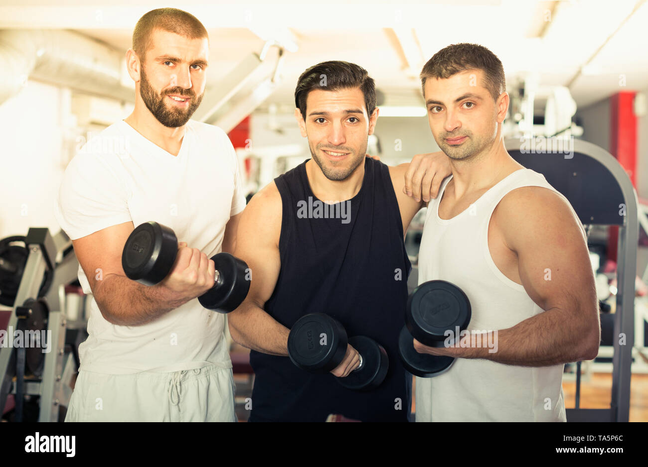 Portrait of three smiling sporty guys during workout in training room ...
