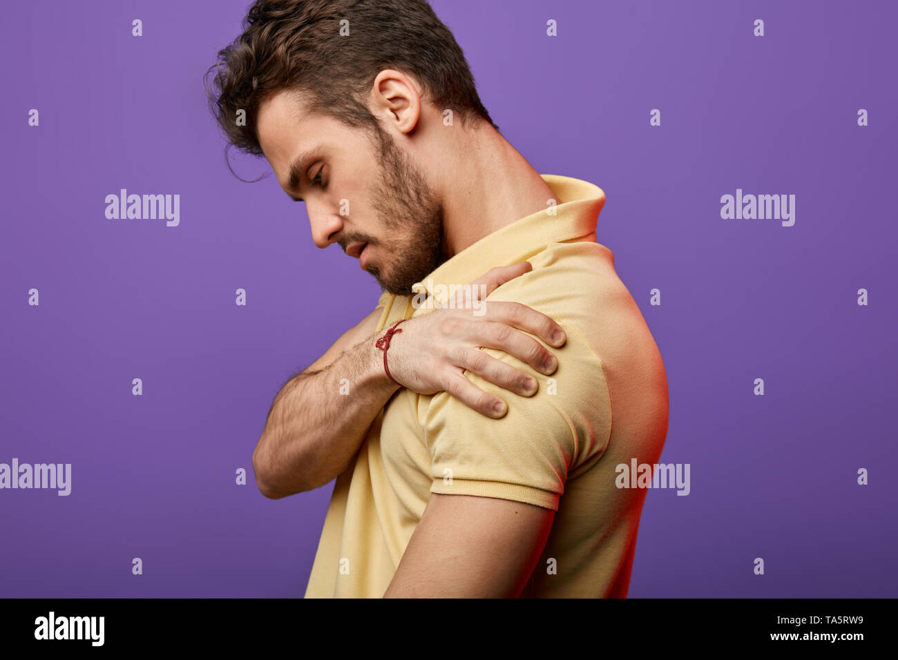young man holding his shoulder and looking down. close up side view ...
