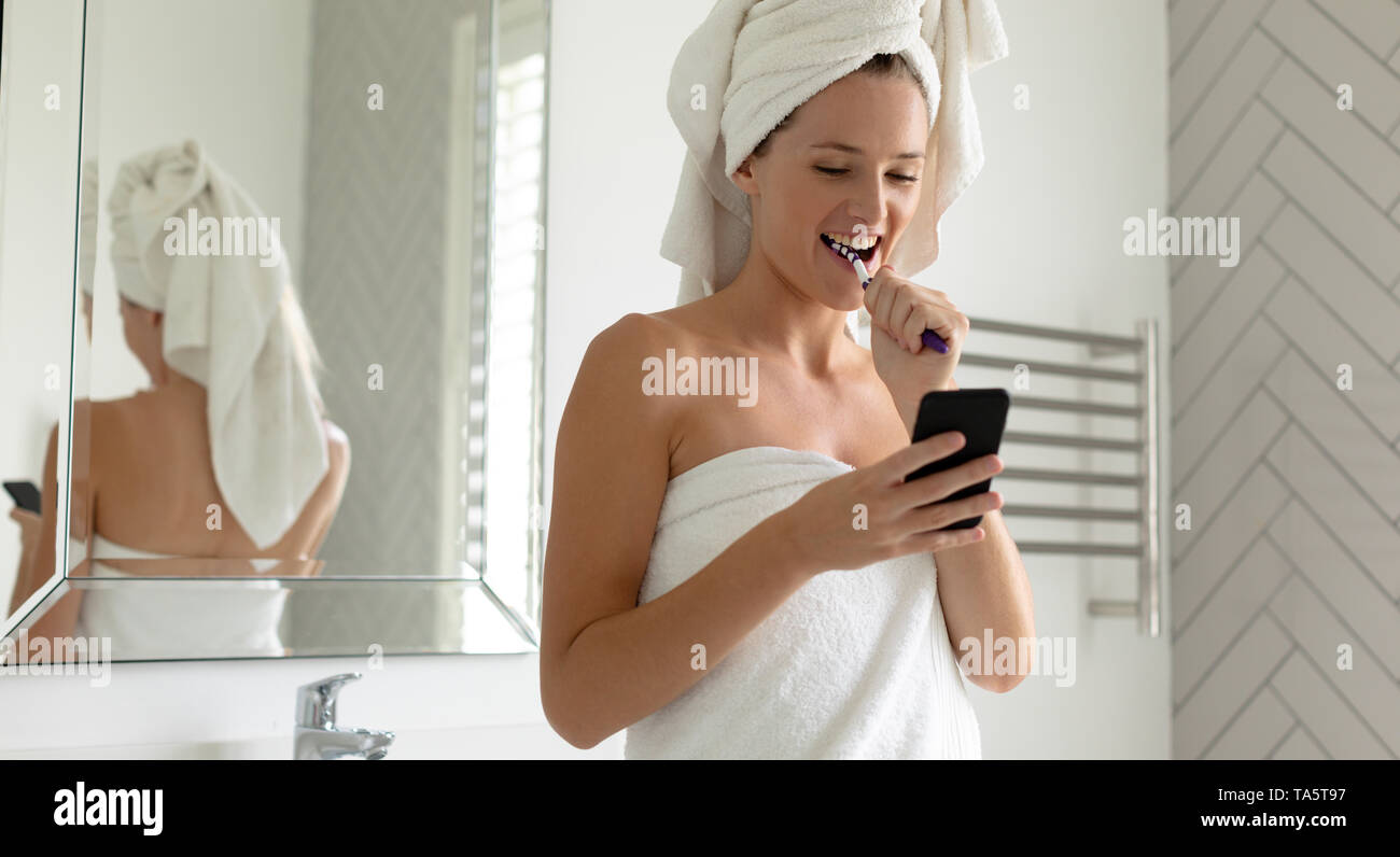 Beautiful woman using her phone while brushing her teeth Stock Photo ...