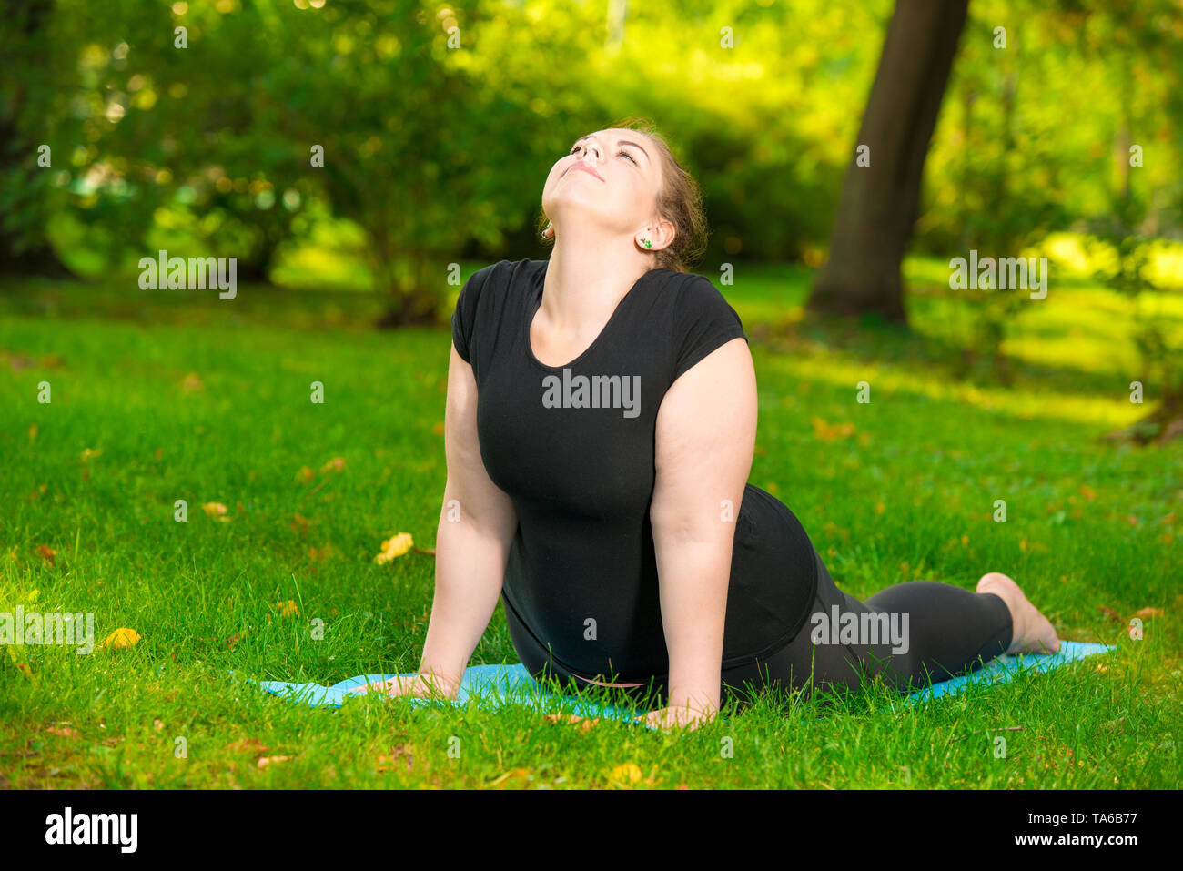 plus size sports woman in park performs stretching exercises, work on ...