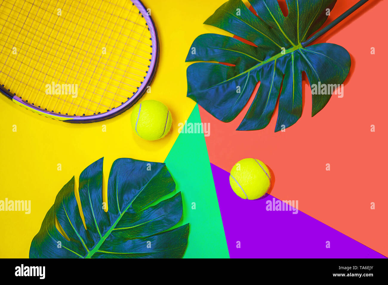 Tennis layout with tennis balls, racket and tropical monstera leaves on ...