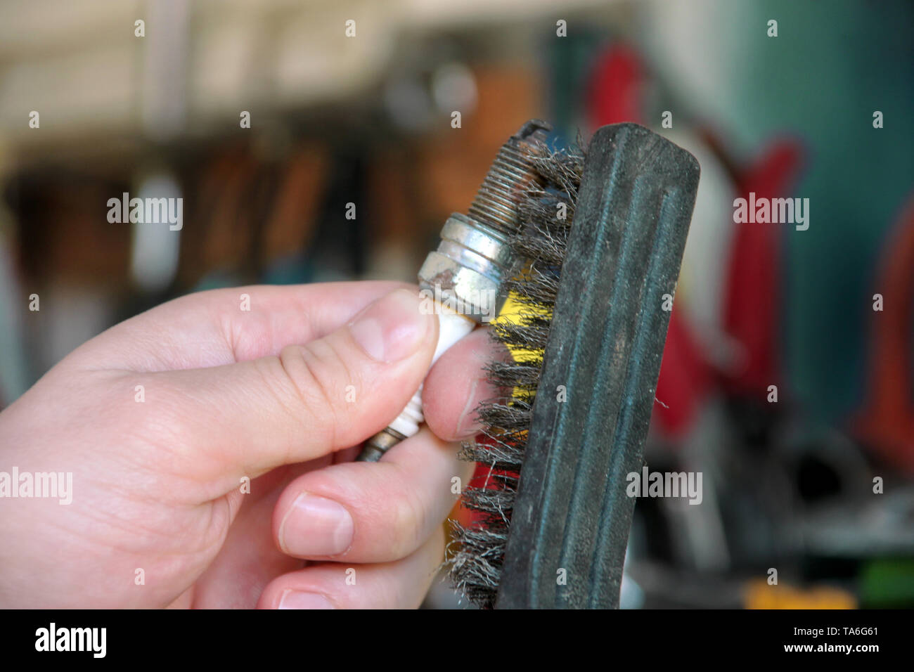 Cleaning a car engine spark plug with wire brush in car garage ...