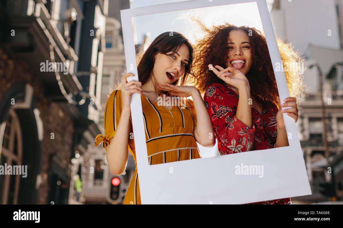 Two women wearing colourful dress standing outdoors holding a photo ...