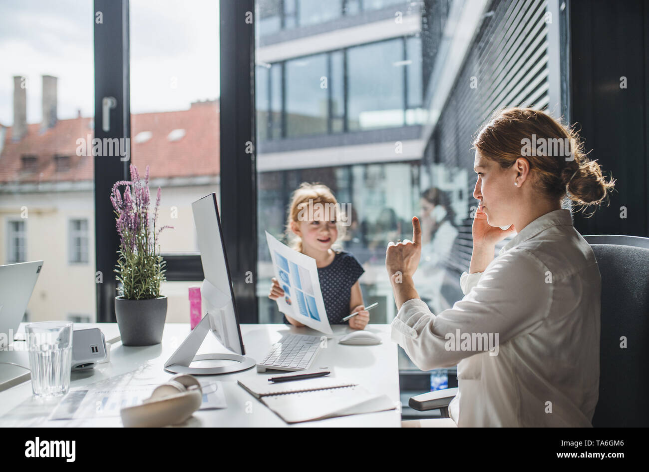 A businesswoman with small daughter sitting in an office, working Stock ...