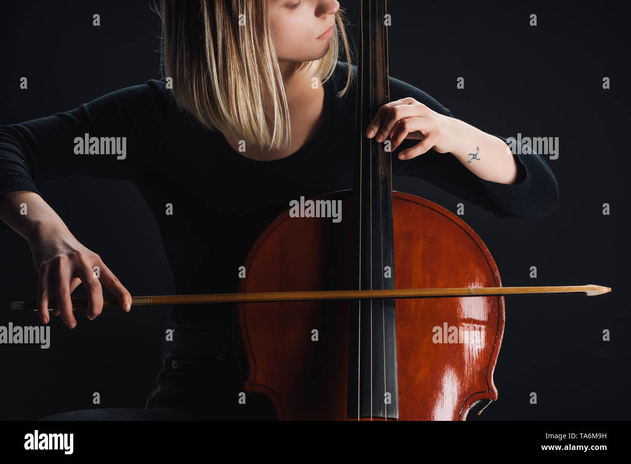 partial view of tattooed woman playing double bass in darkness isolated ...