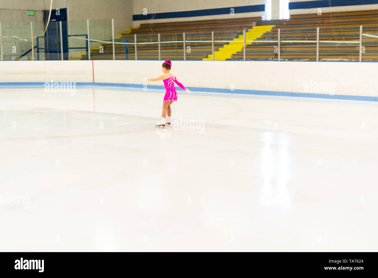 Little figure skater in pink dress practicing on the indoor ice rink ...