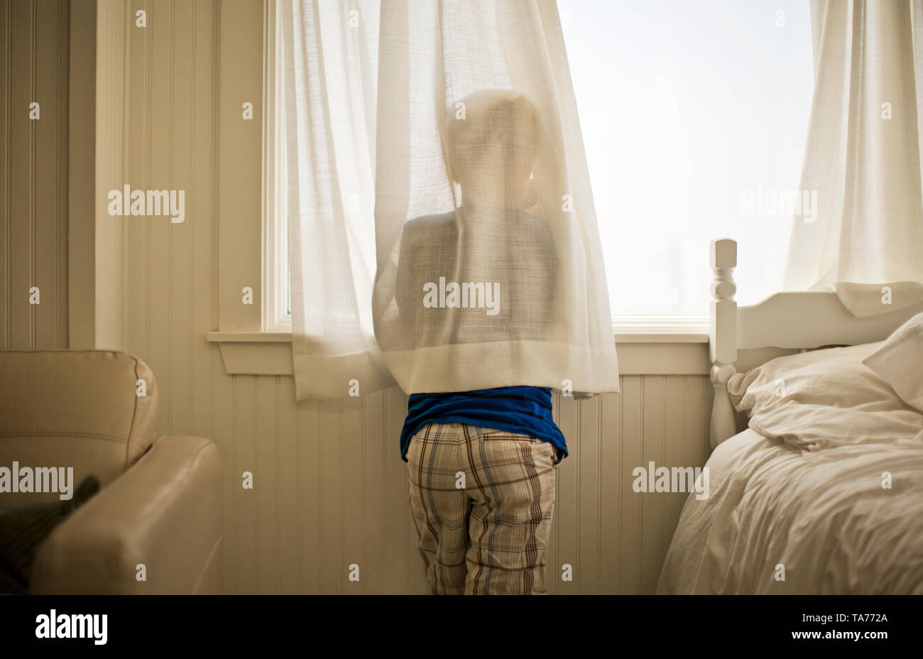 Young boy standing in a bedroom and looking out a window Stock Photo ...