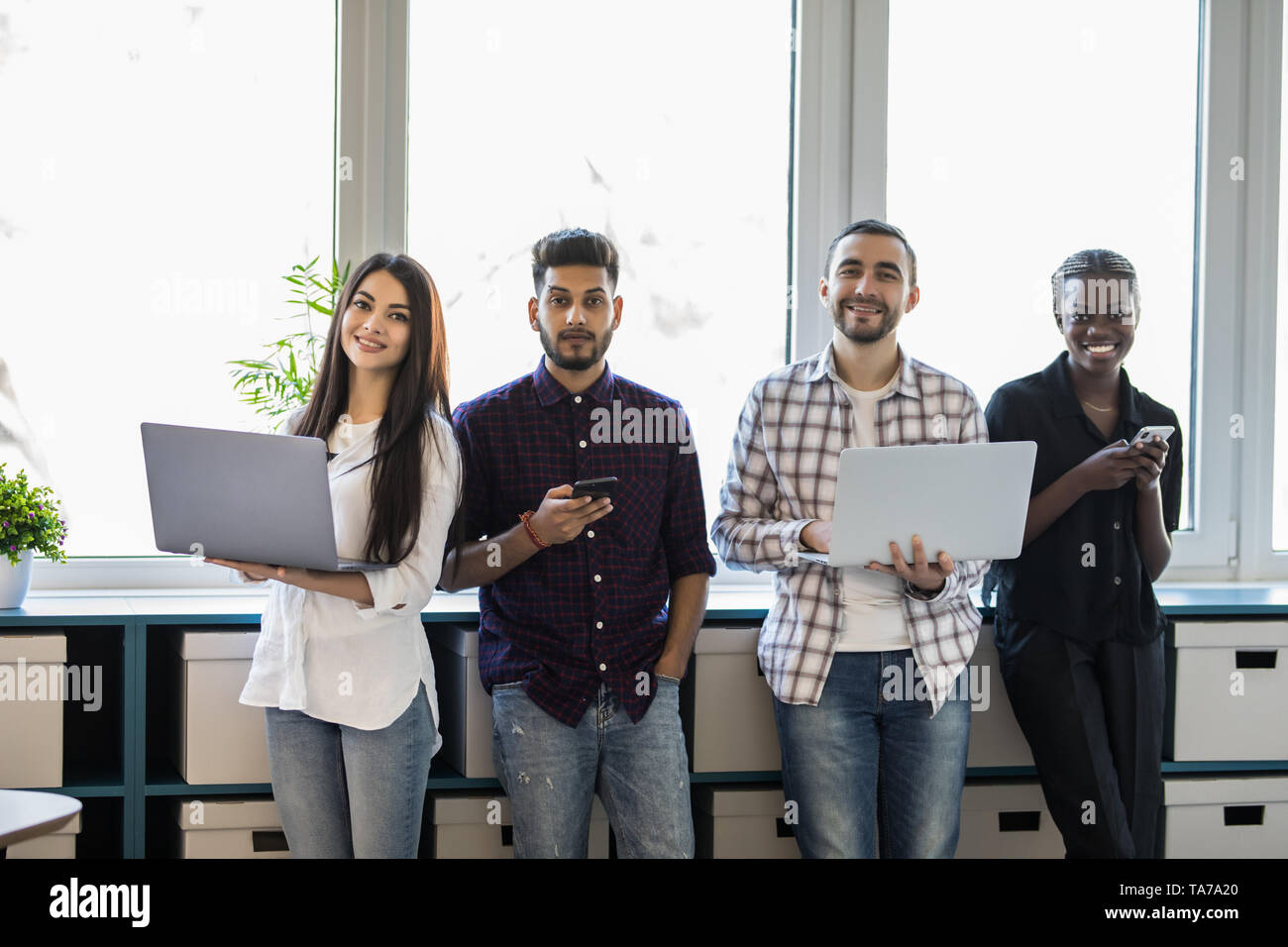 Young team standing with devices in modern office Stock Photo - Alamy