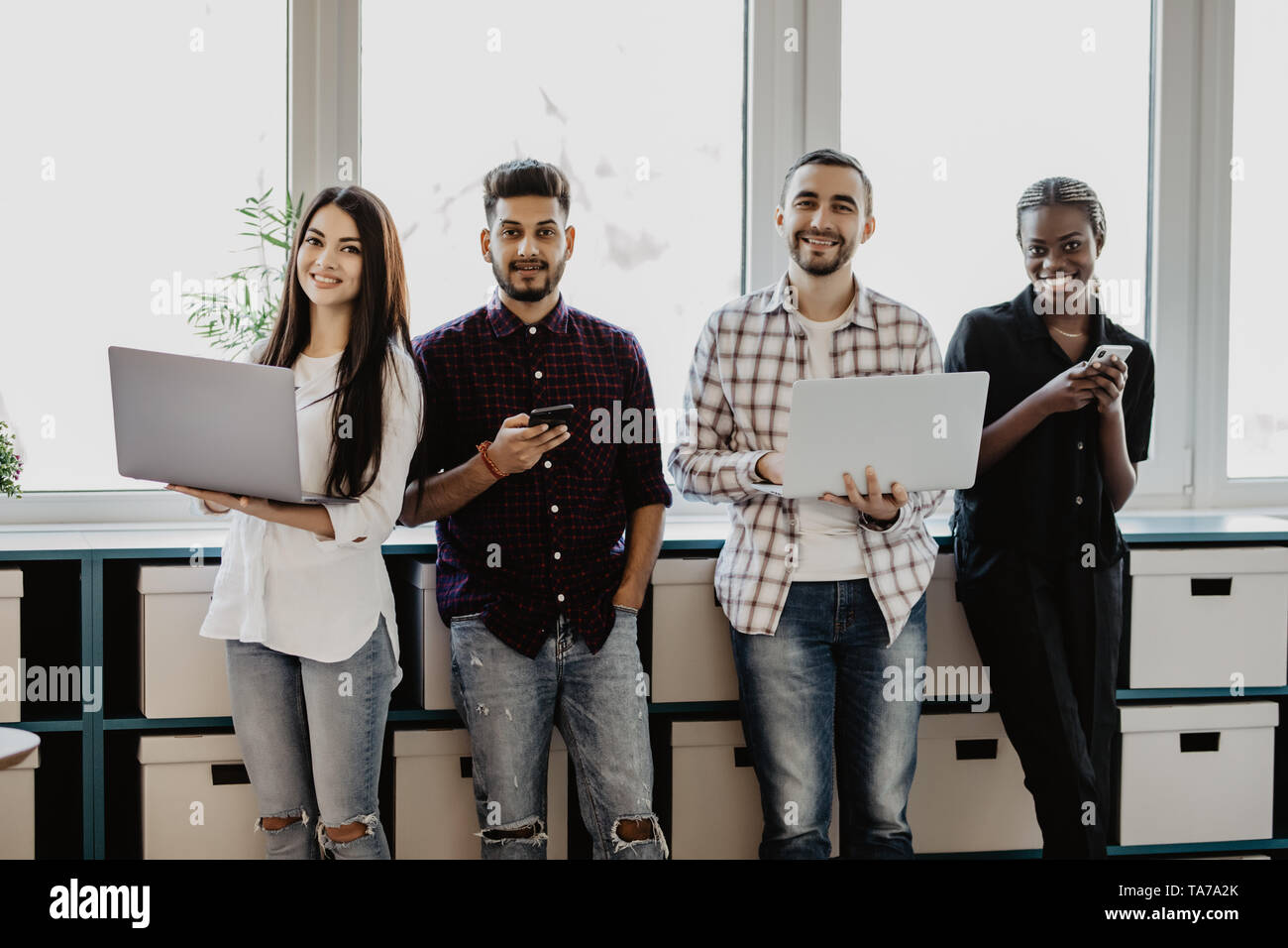 Young team standing with devices in modern office Stock Photo - Alamy