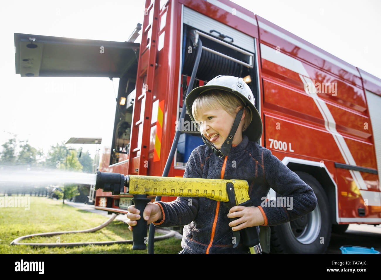 Little boy acting like a fireman holding firehose nozzle and splashing ...