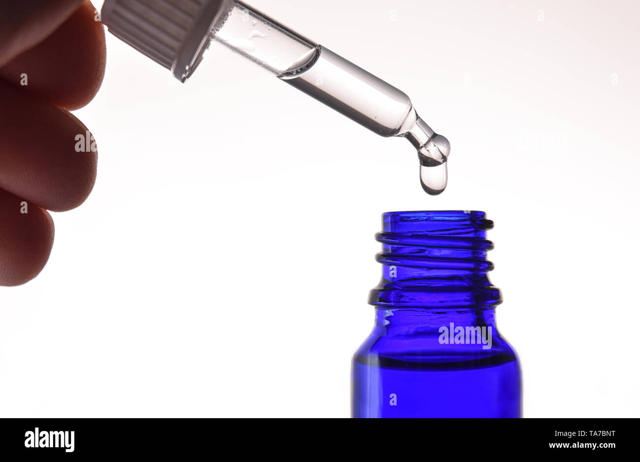 Hand putting drops from a dropper in a blue jar full of liquid close up ...