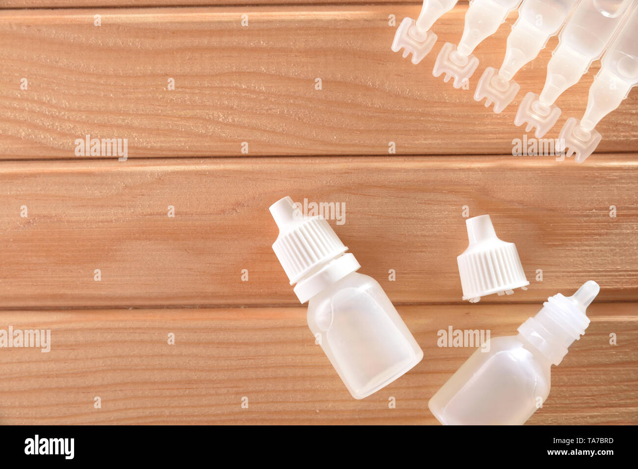 Several pipettes of eye drops and jars on wood table. Horizontal ...