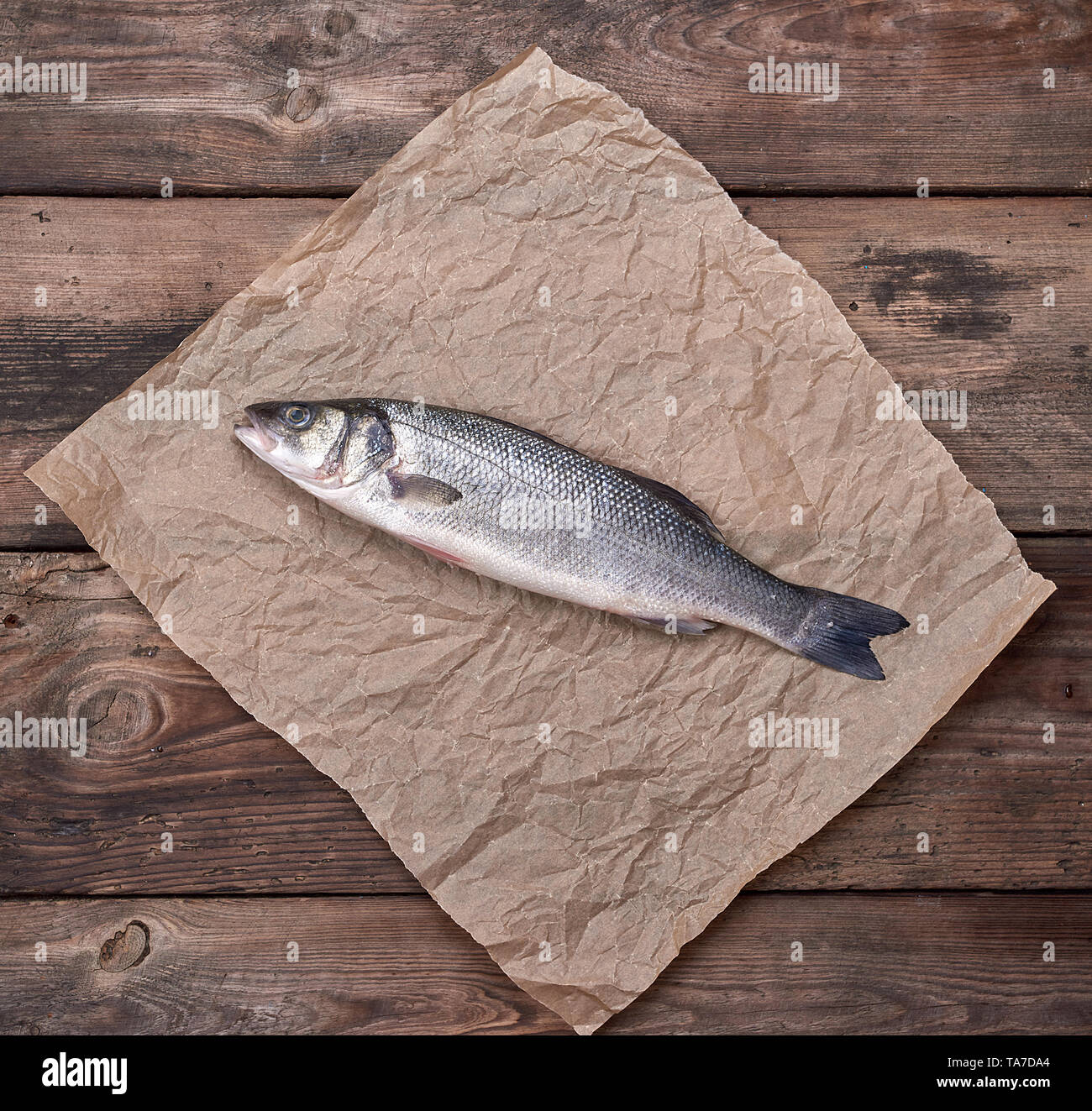 fresh whole sea bass fish on brown crumpled paper, top view, copy space ...