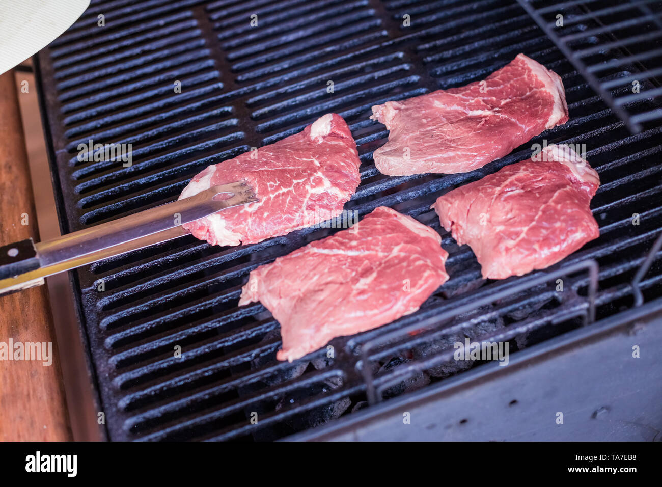Man placing raw meat on to a hot barbecue to grill using a pair of ...