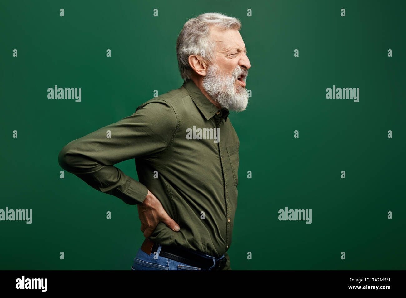 angry shouting old man suffering from back pain isolated on green ...
