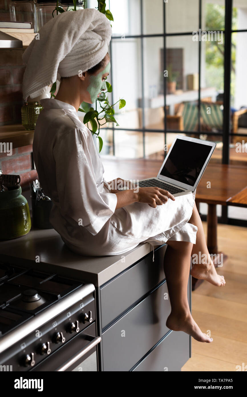 Woman in bathrobe sitting on the kitchen counter and using laptop Stock ...