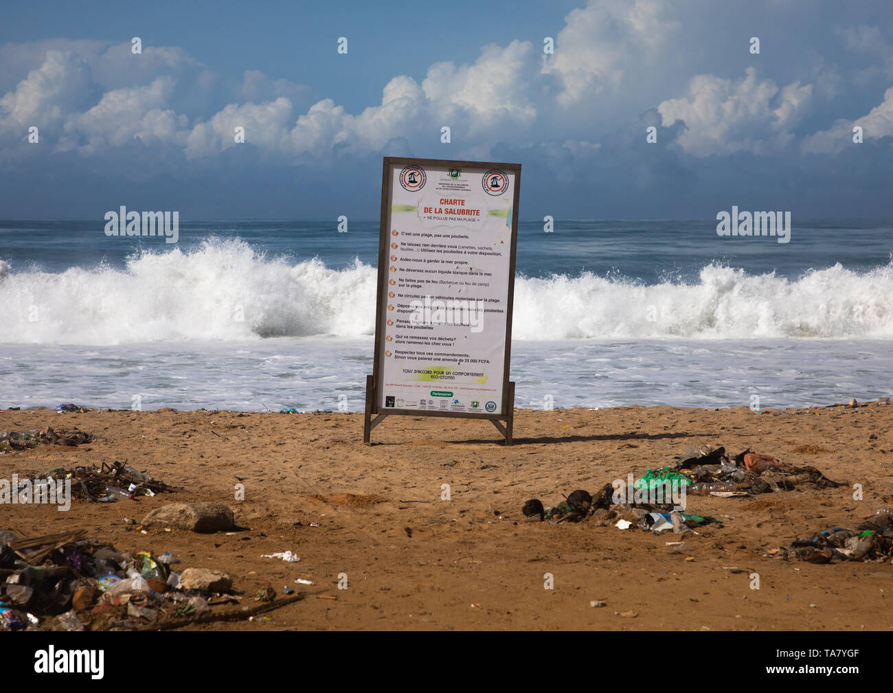 Garbage on the beach in front of a billboard to fight against pollution ...
