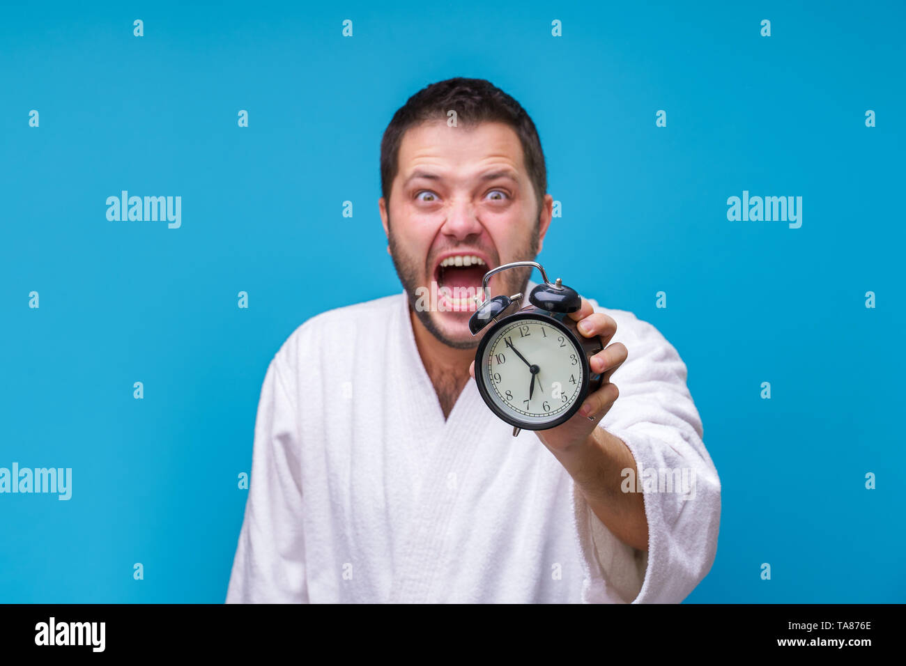 Photo of screaming man with alarm clock in hand on empty blue ...