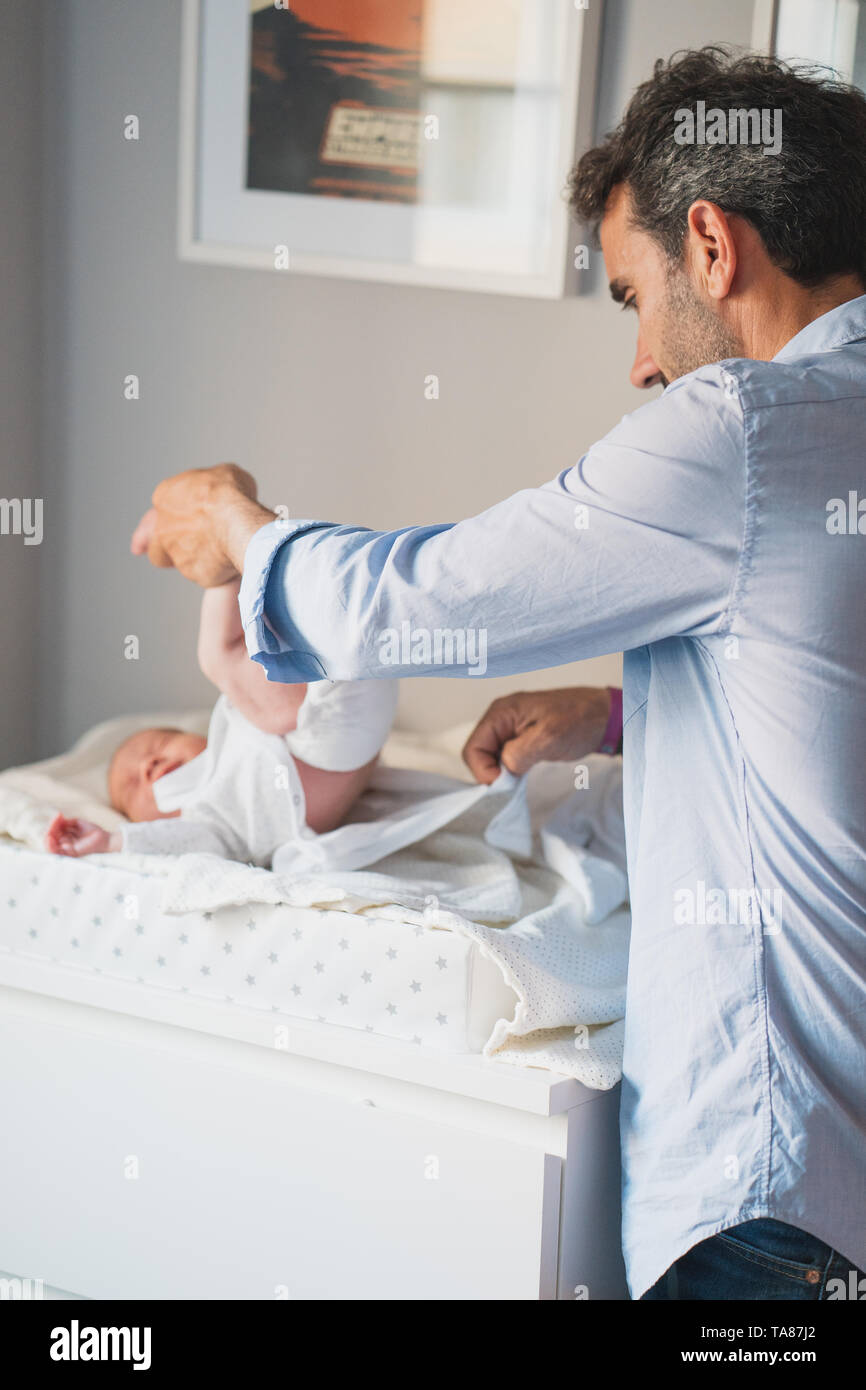 New father changing the diaper to his cute newborn. Baby expresses calm ...