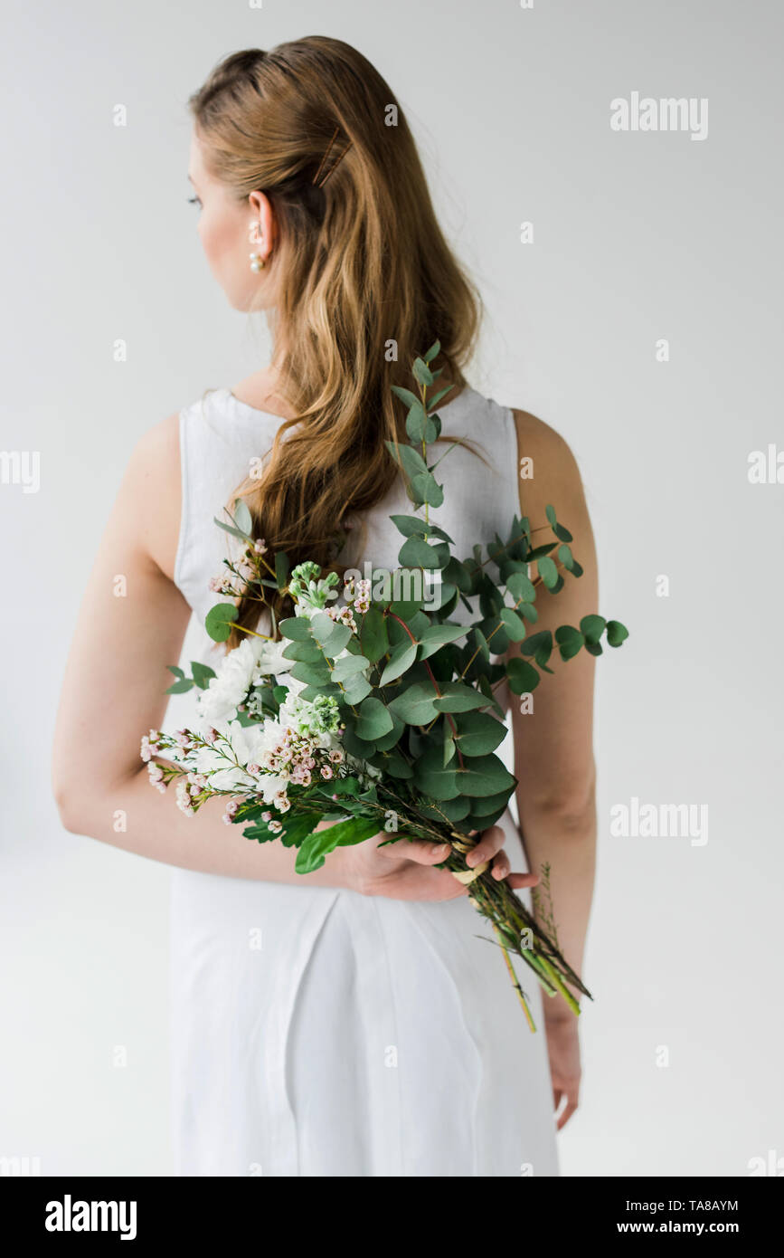 back view of girl in elegant dress holding flowers behind back isolated ...