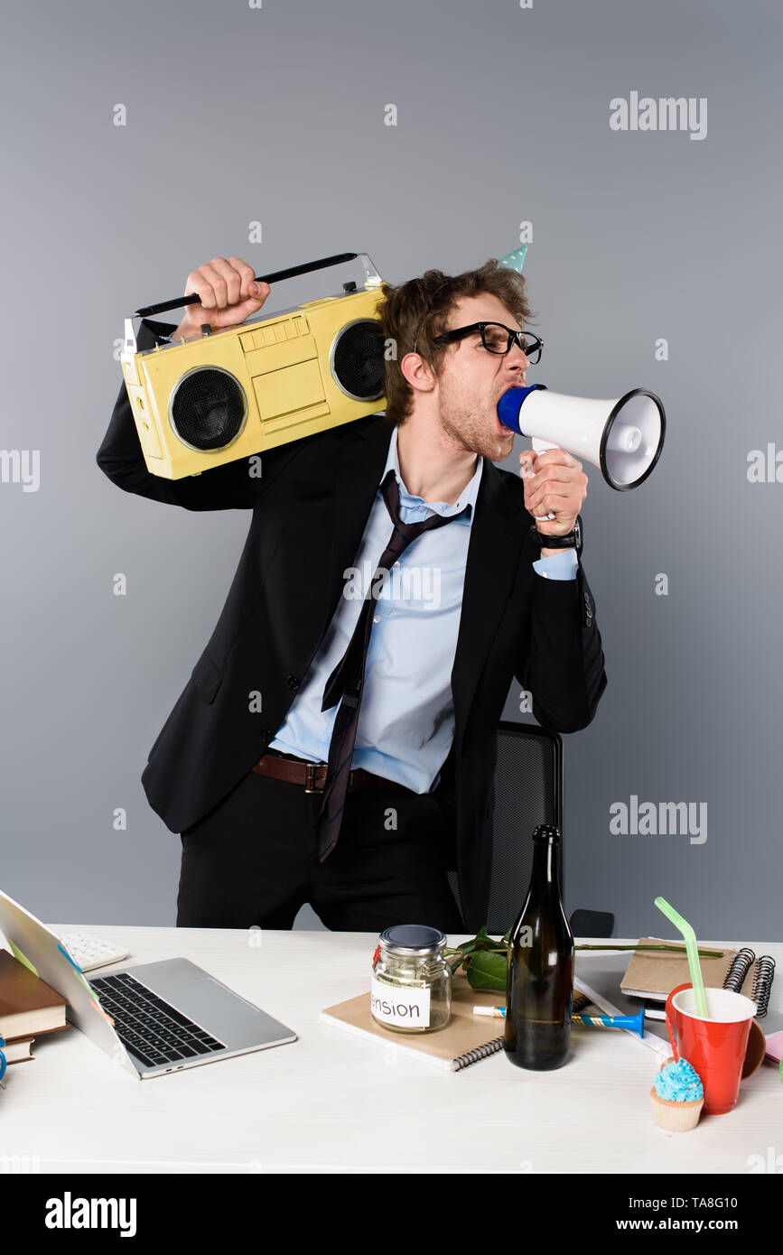 angry businessman at workplace in party cap holding vintage tape ...