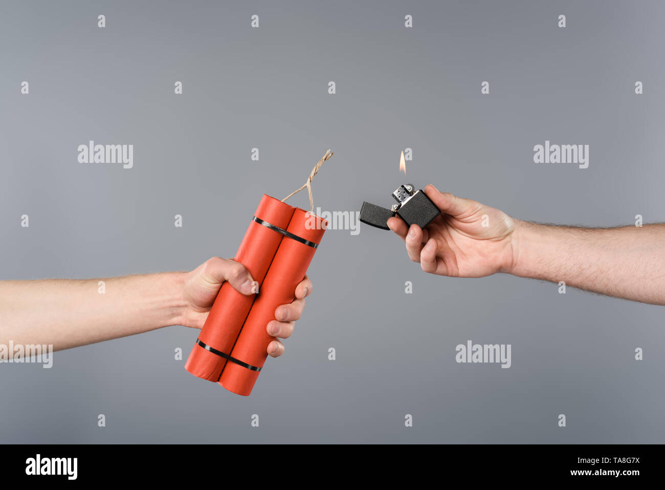 cropped view of men holding dynamite and lighter on grey background ...