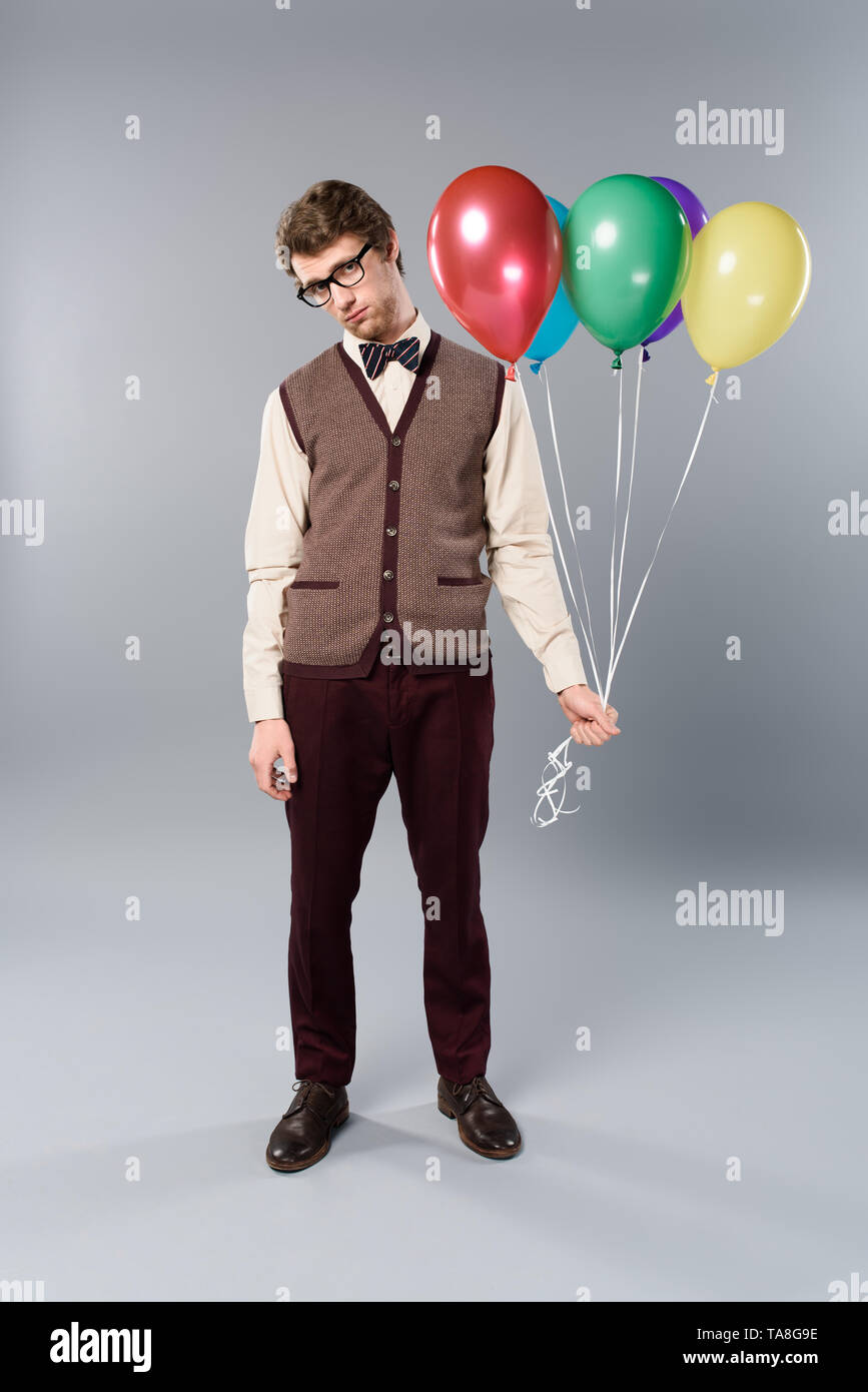 sad man in glasses holding multicolored balloons on grey background ...