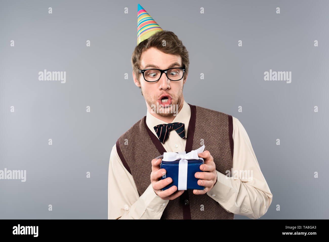 shocked man in party cap holding gift box on grey Stock Photo - Alamy