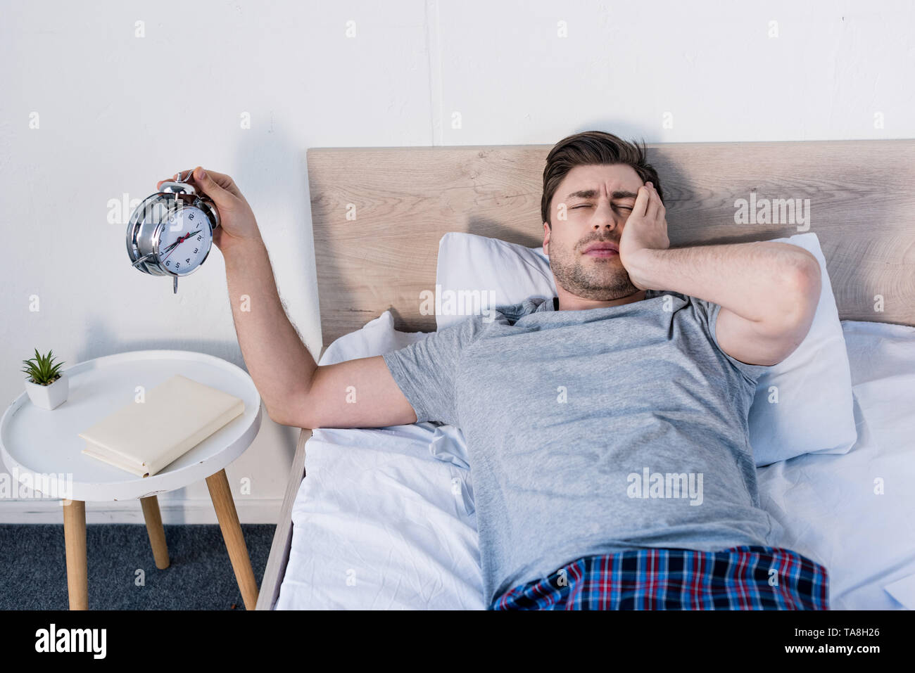 overslept man with closed eyes holding alarm clock while laying on bed ...