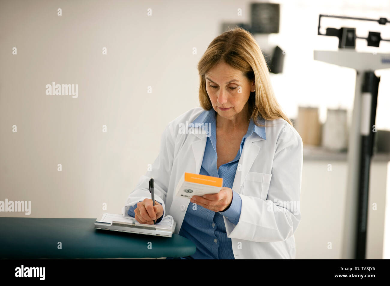 Mid adult doctor taking notes while reading a box of medical supplies ...