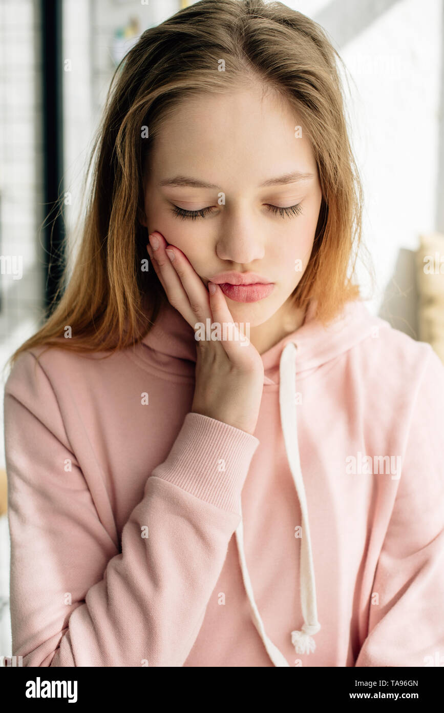 Tired teenage kid in pink hoodie touching face with closed eyes Stock ...