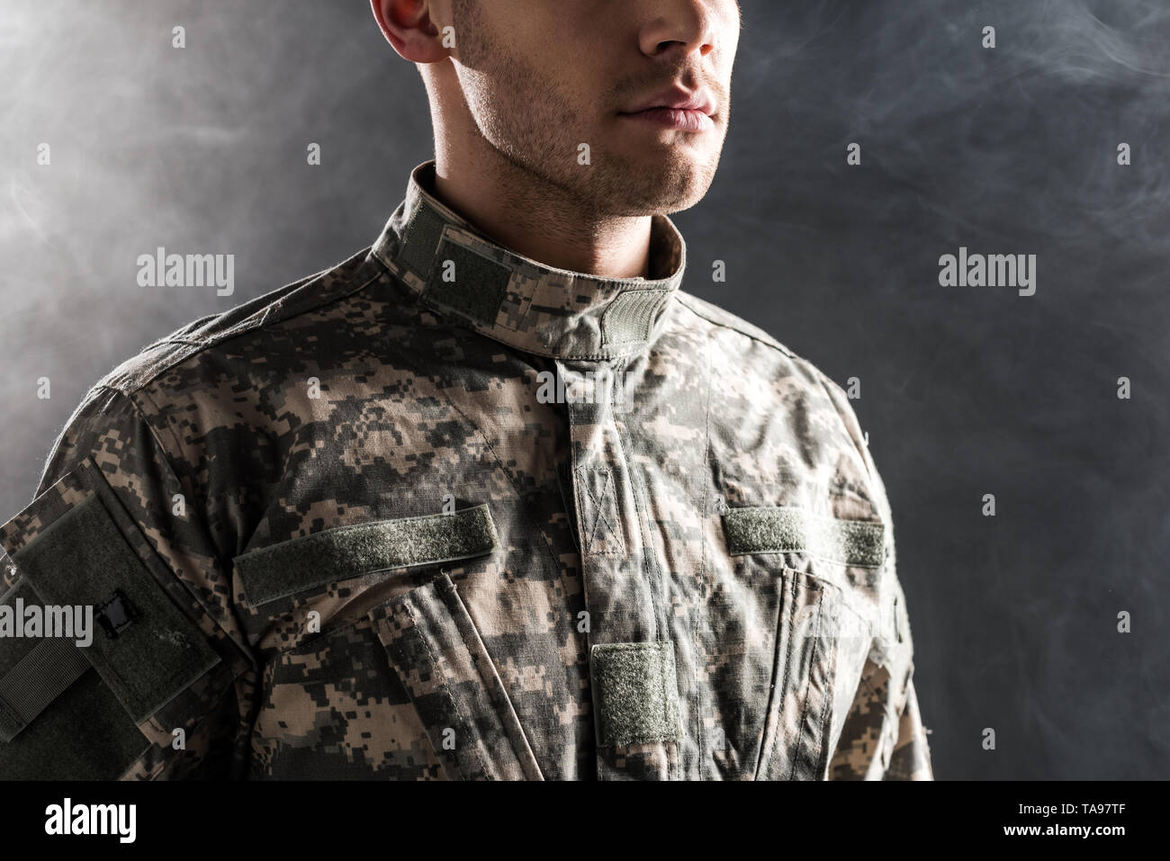 cropped view of serious soldier in military uniform on black with smoke ...