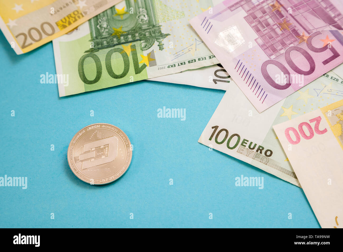 Silver Dash coin next to Euro bank notes on blue background. Digital ...