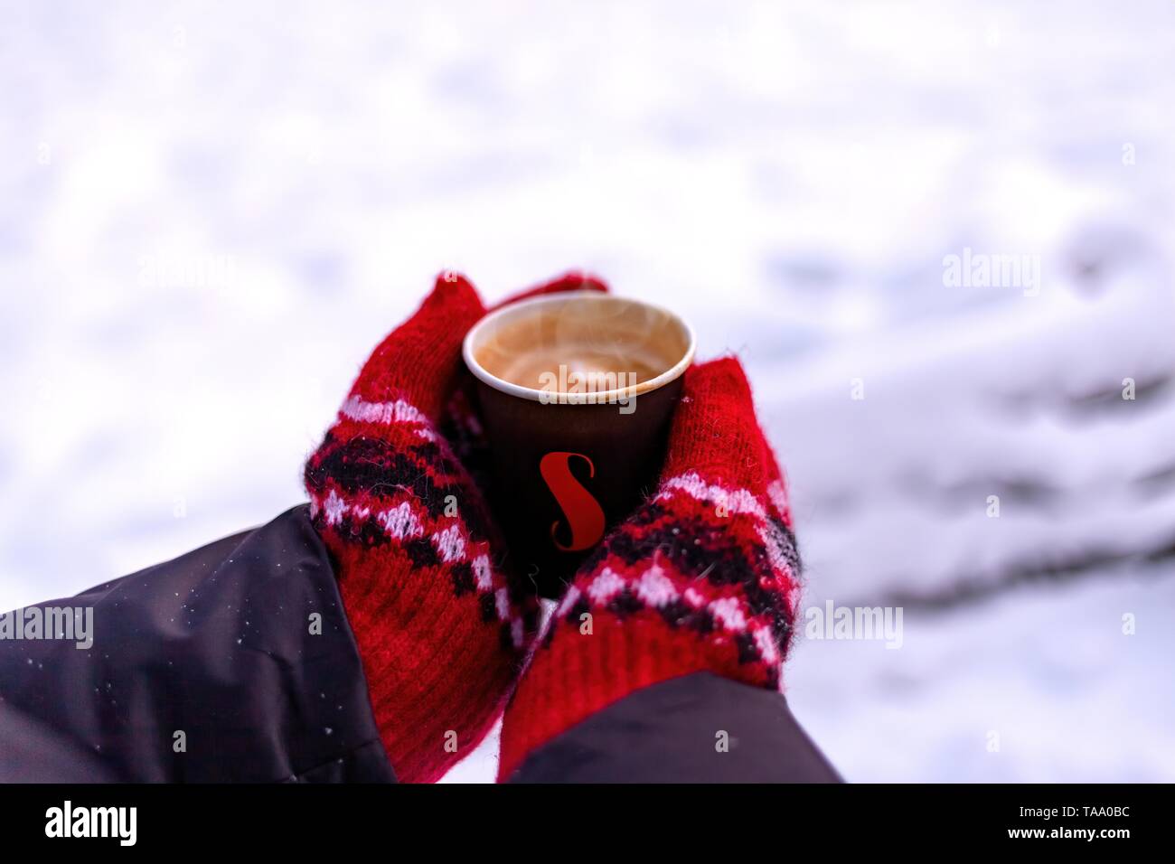 Women's hands in a red mittens hold a paper cup of coffee. Back side ...