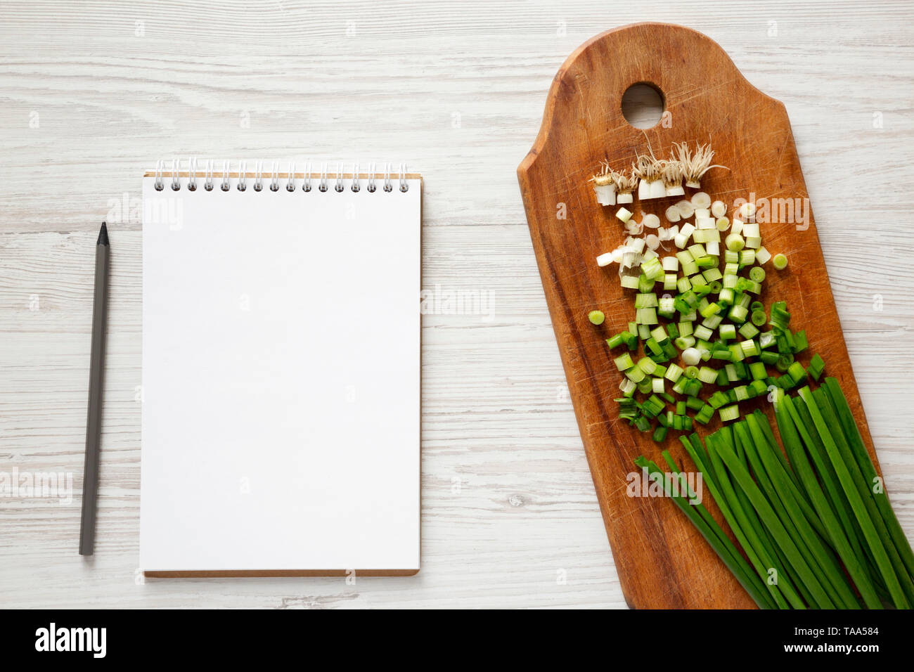 Chopped green onions on a rustic wooden board, blank notepad with ...