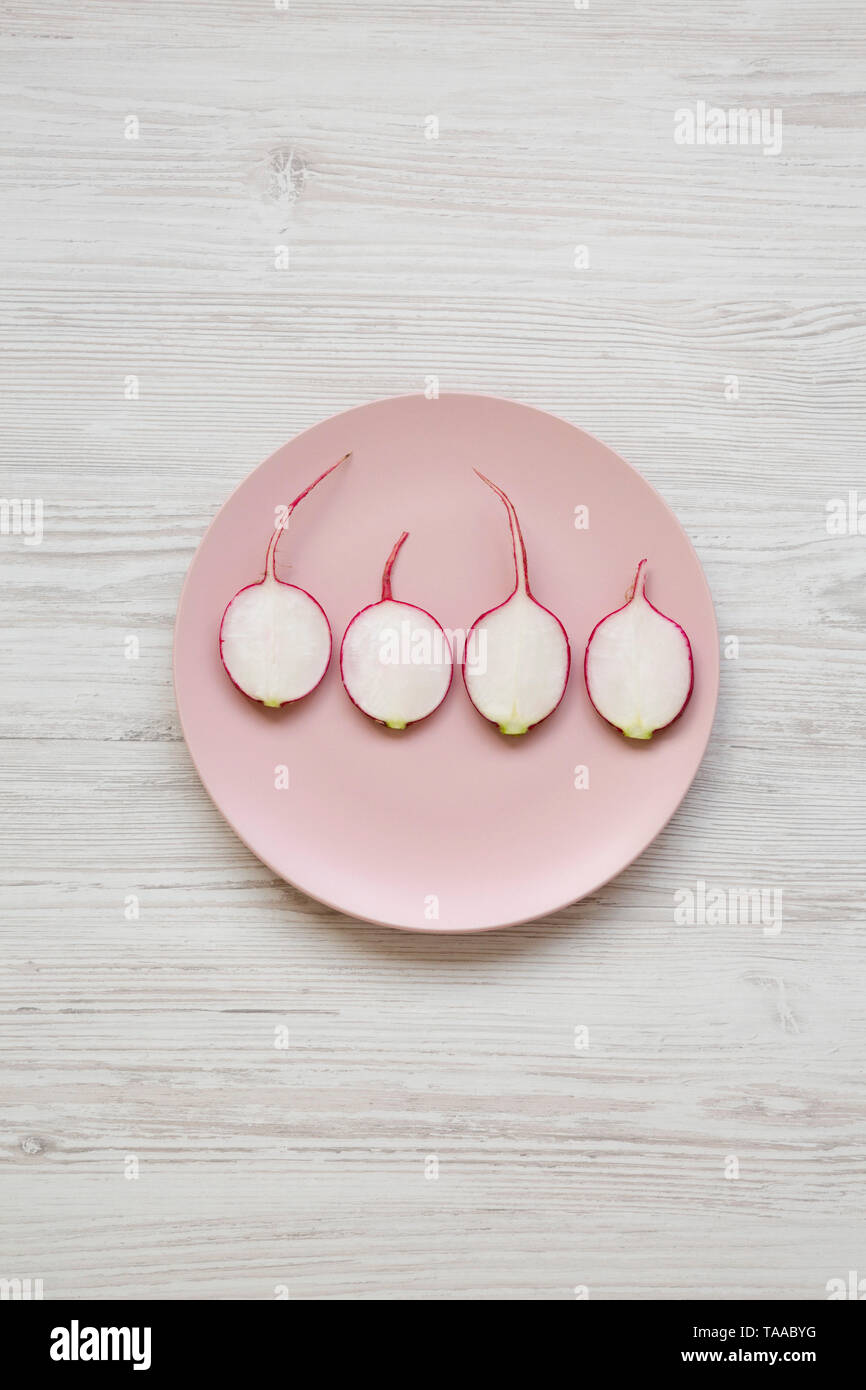Radish slices on a pink plate over white wooden background, top view ...