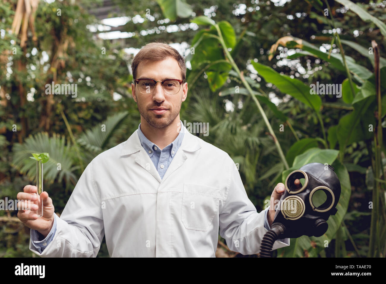 handsome scientist in white coat and glasses holding rubber gas mask ...