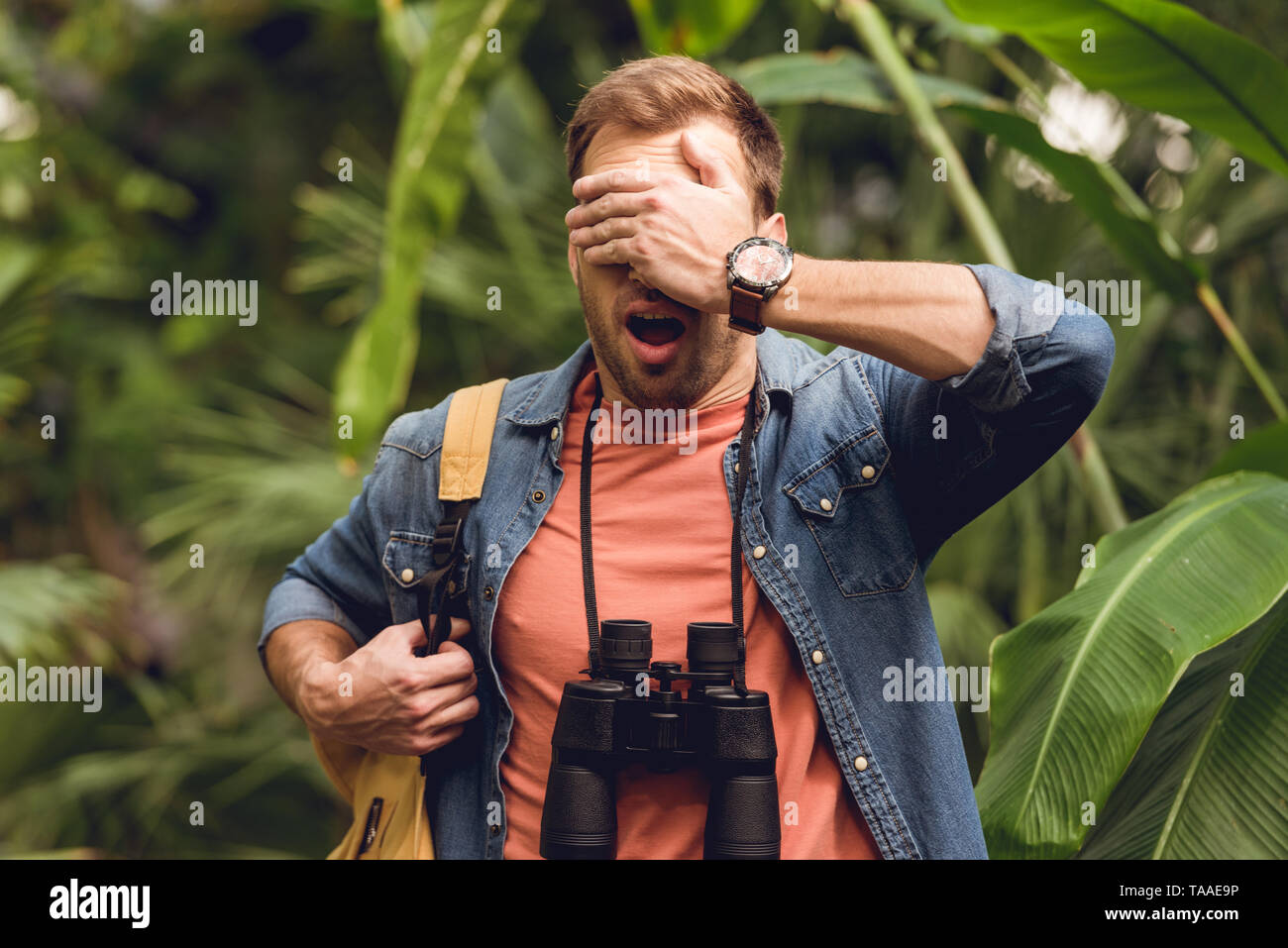 handsome scared traveler with binoculars and backpack putting hand on ...