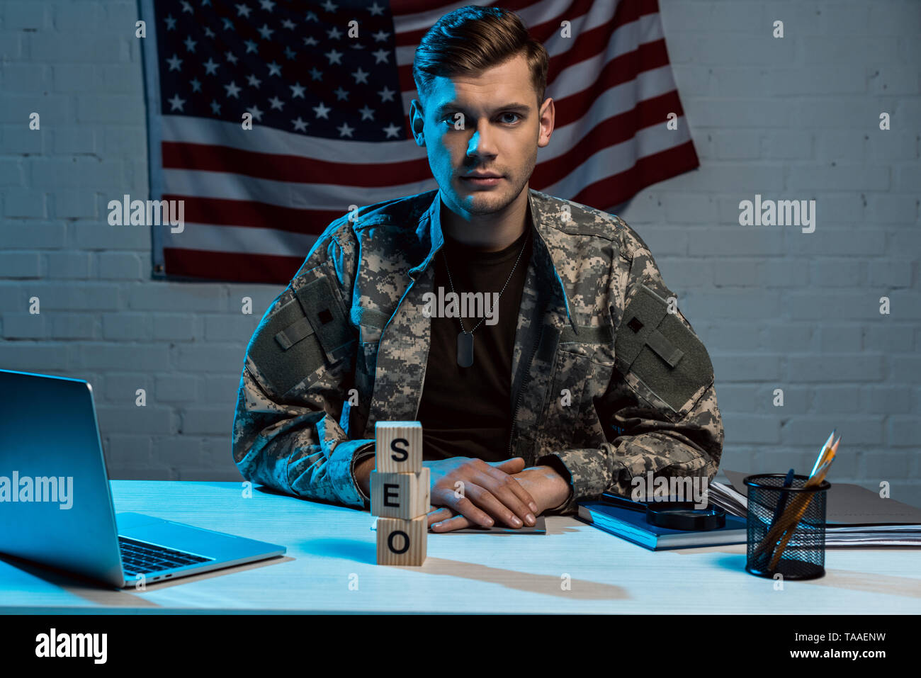 handsome military man sitting with clenched hands near laptop and cubes ...