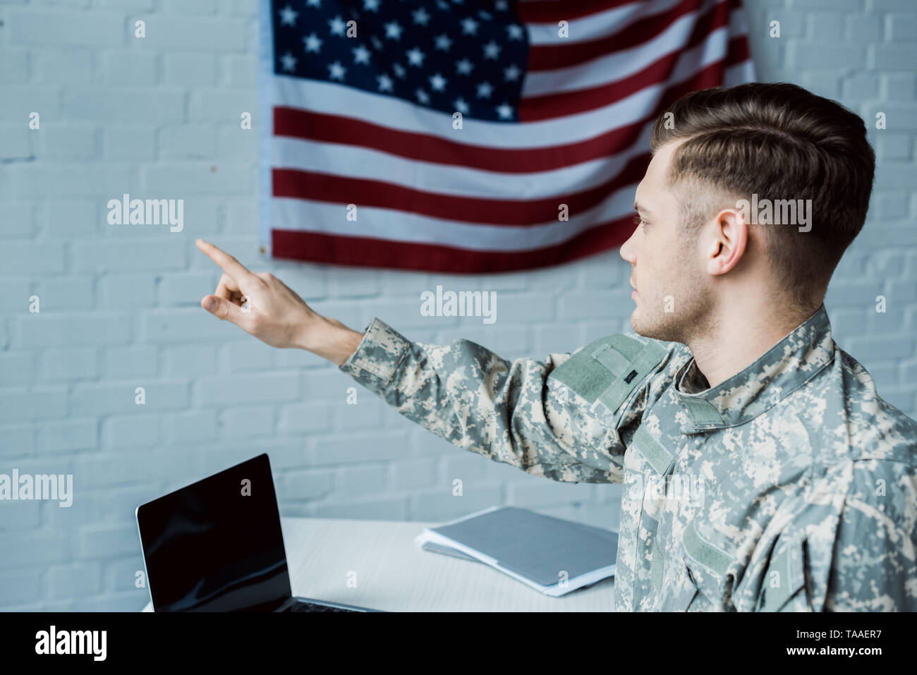 handsome military man pointing with finger in office near laptop with ...