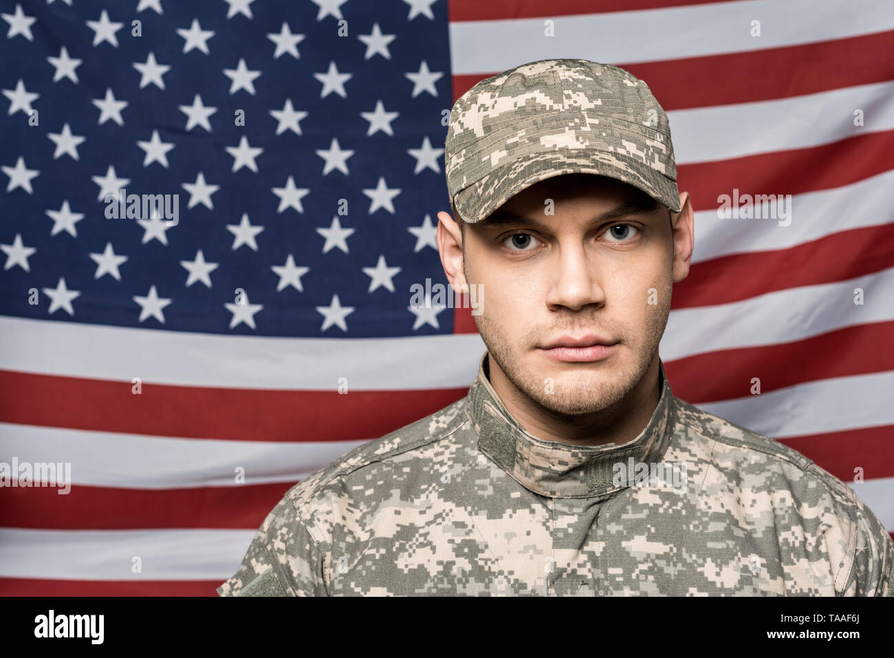 handsome soldier in military uniform and cap looking at camera near ...