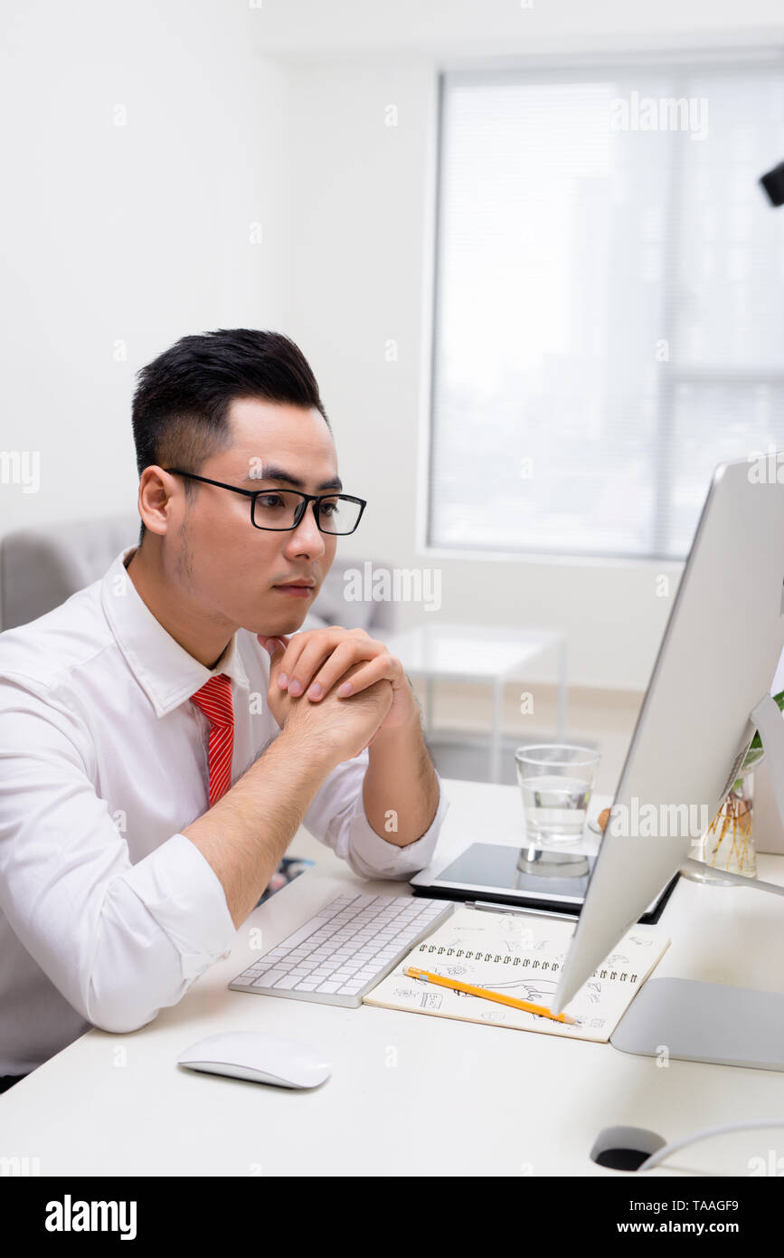 Young stylish worker at office working with computer and thinking how ...
